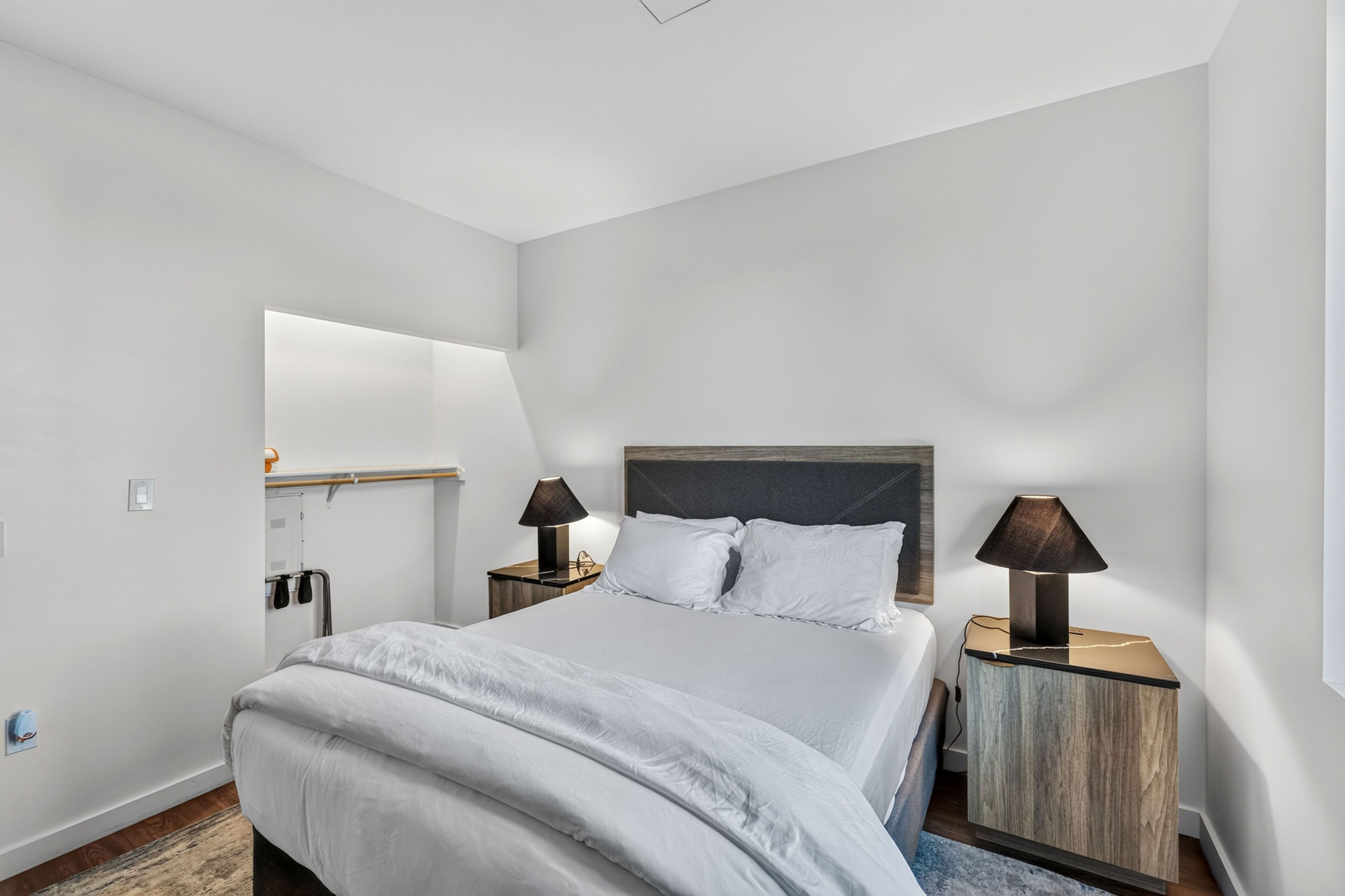 Um quarto com uma cama, duas mesas de cabeceira com luminárias, uma cabeceira de madeira e um espelho grande na parede.