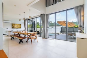 Um quarto amplo com uma mesa de jantar grande, um sofá e vista para o exterior por grandes janelas.