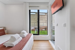 Quarto de hotel com cama, televisão, janela com vista para uma varanda e porta deslizante.