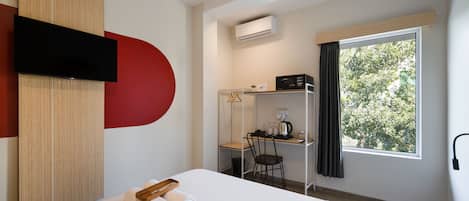 Quarto de hotel com cama, escrivaninha, cadeira, ar condicionado, janela com vista e design de parede em vermelho e branco.