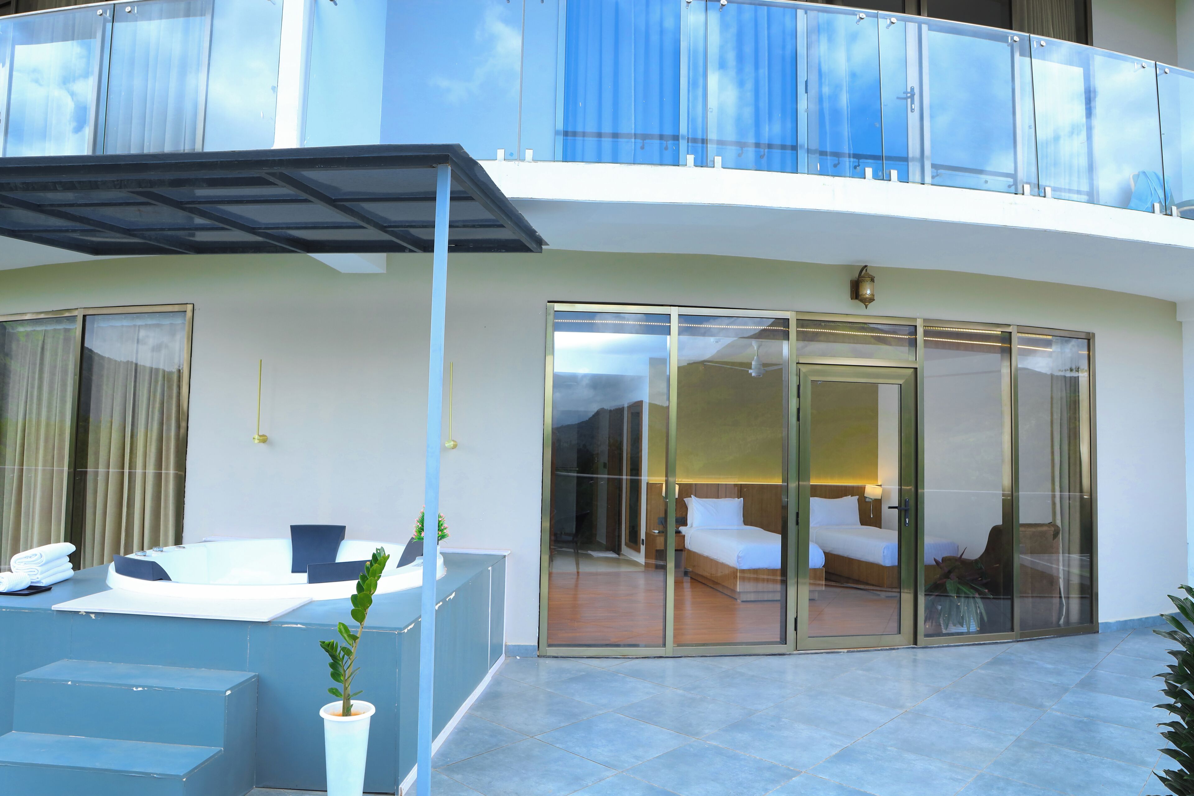 Um hotel moderno com varanda envidraçada, área de recepção e quarto com cama grande e mesa de cabeceira.