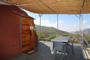 Uma área externa coberta com mesa e cadeiras, um edifício de madeira e vista para colinas.