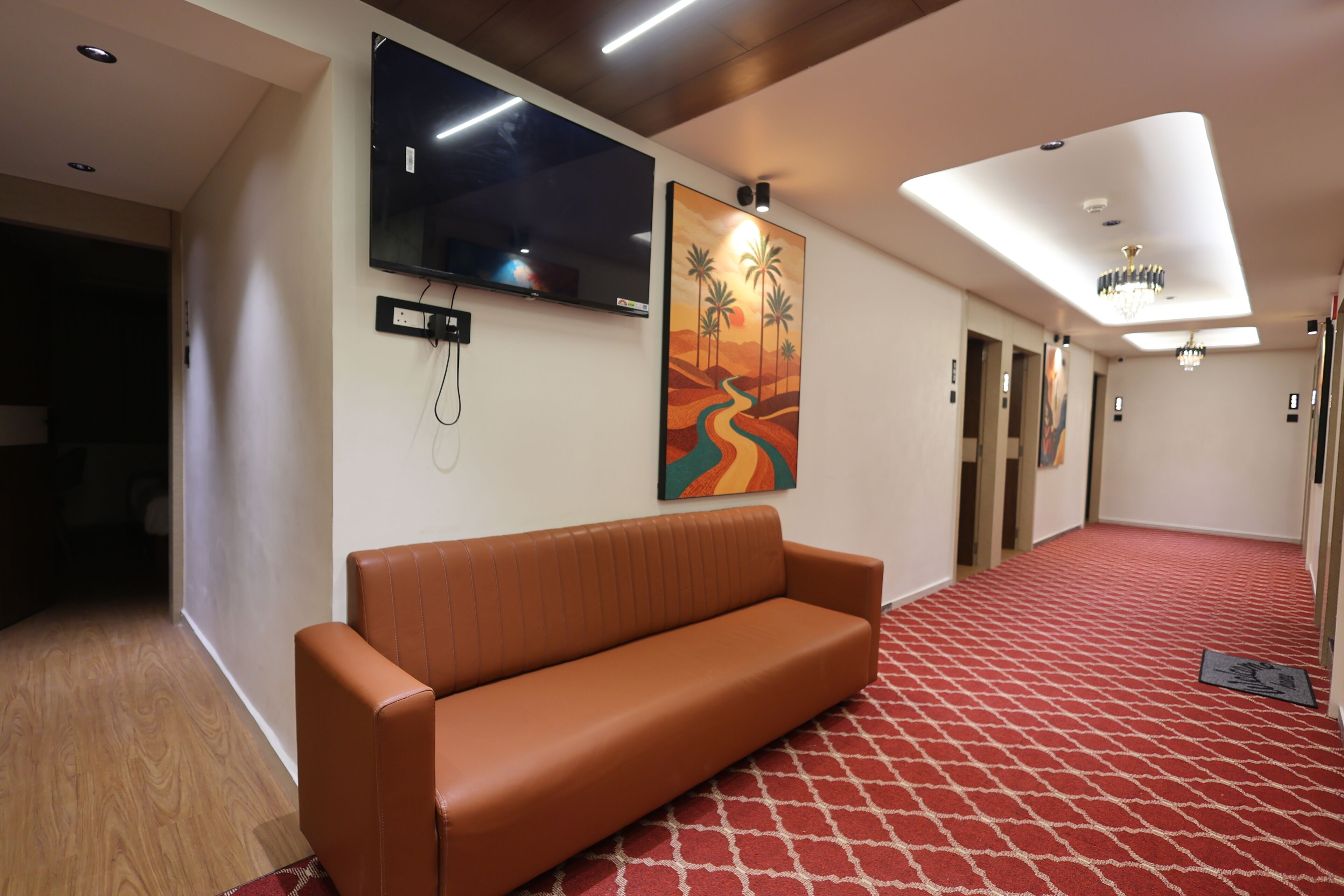Um saguão de hotel com um sofá, uma televisão de tela plana, uma pintura de palmeiras e um tapete vermelho estampado.