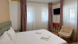 Quarto de hotel com uma cama grande, uma cadeira, uma televisão e cortinas.