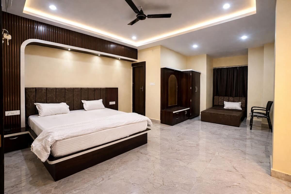 Quarto moderno com cama grande, guarda-roupa, área de estar e ventoinha no teto.