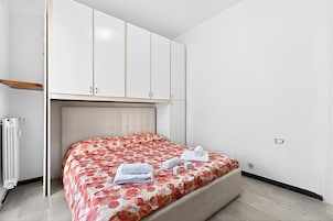 Quarto com cama, guarda-roupa branco e radiador.