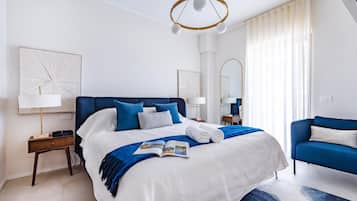 Quarto de hotel moderno com uma cama grande, duas mesas de cabeceira, uma escrivaninha, uma cadeira, um espelho grande e um candelabro.