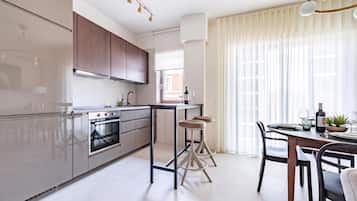 Cozinha moderna com forno embutido, área de refeições com mesa e cadeiras, e uma janela grande com cortinas.
