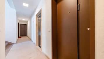 Um corredor com piso coberto por carpete, porta com fechadura eletrônica e luminária fixada na parede.