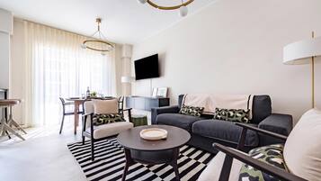 Uma sala de estar moderna com sofá, cadeiras, mesa de centro, televisão e área de jantar com mesa e cadeiras.