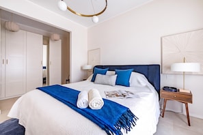 Quarto moderno com cama grande, abajures, mesa de cabeceira e um detalhe decorativo na parede.