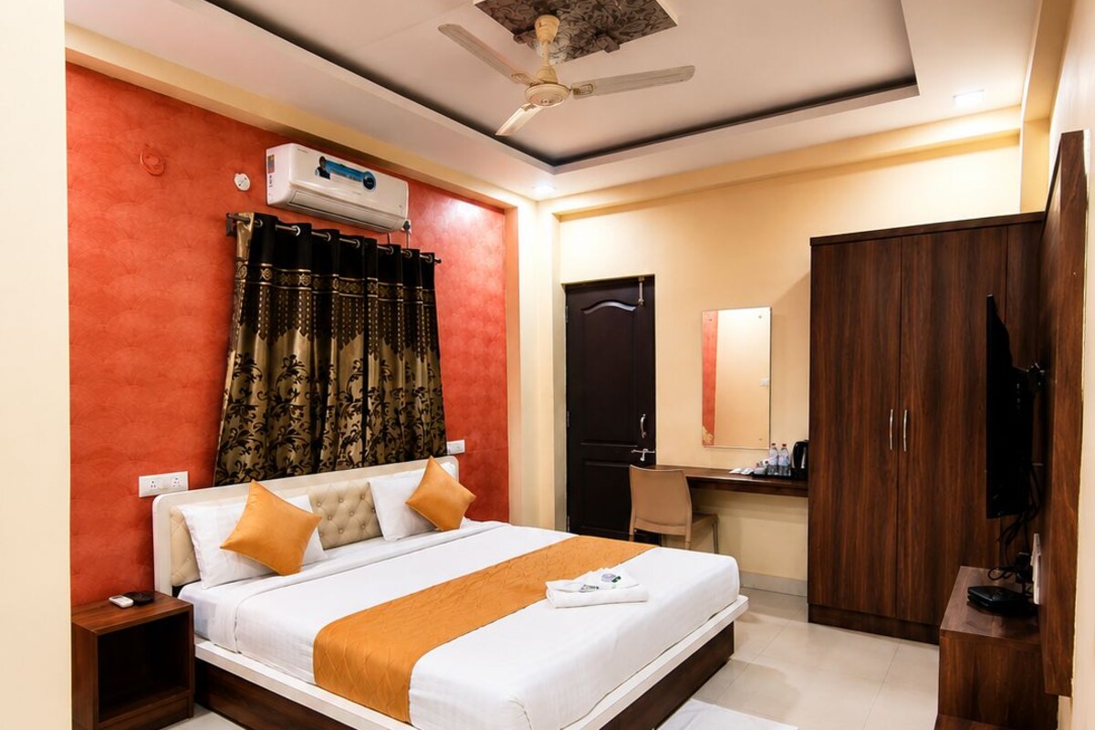 Quarto de hotel com cama, guarda-roupa, escrivaninha e televisão.