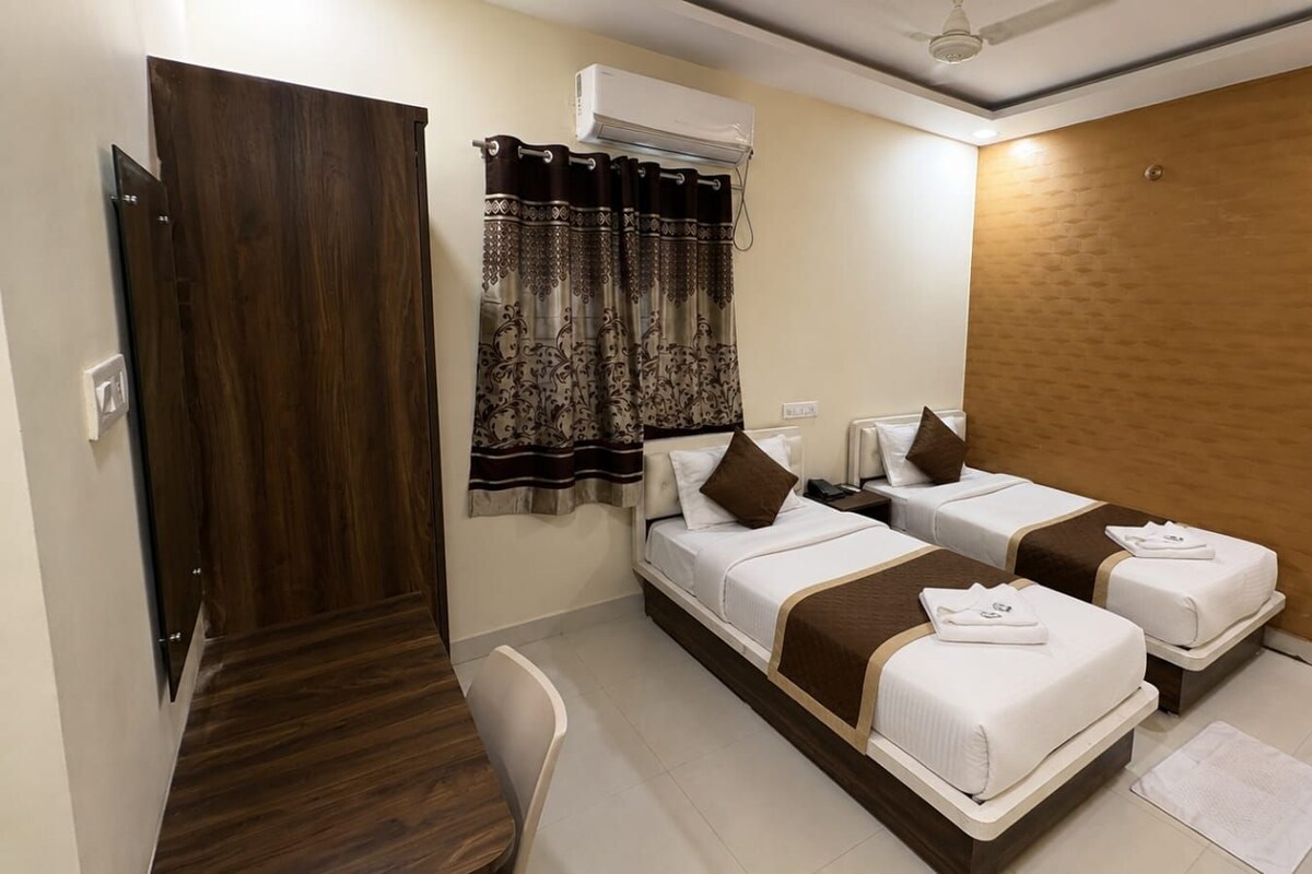 Quarto de hotel com duas camas, uma escrivaninha, uma cadeira, ar condicionado e televisão.