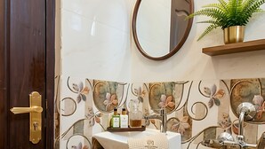 Um banheiro com pia de mármore, espelho redondo, planta em vaso e decoração na parede.