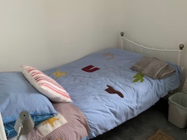 Uma cama de solteiro com colchão azul, cabeceira branca e lixeira cinza.