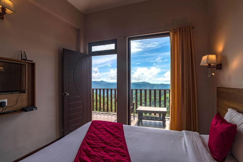 Quarto de hotel com cama, televisão, varanda e vista para as montanhas, e porta que dá para o exterior.