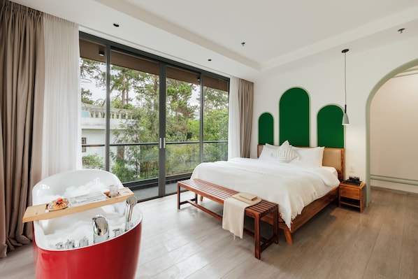 Quarto de hotel moderno com uma janela grande, uma cama de madeira, uma banheira vermelha e um banco.