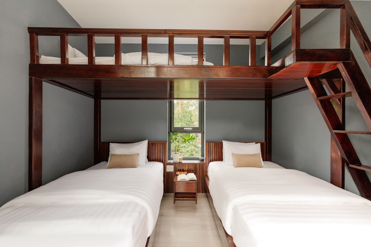 Quarto com duas camas, uma janela e escada de madeira.