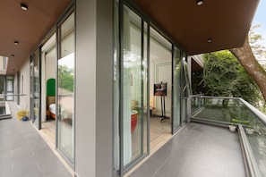Quarto de hotel moderno com grandes portas de vidro, uma varanda com guarda-corpo e vista para o exterior.