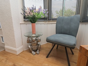 Quarto de canto com uma poltrona cinza, uma mesa de vidro com um vaso rosa e uma escultura de macaco.