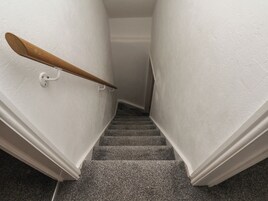 Uma escadaria estreita com corrimão de madeira e degraus carpetados.