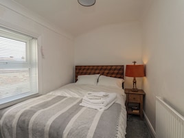 Quarto com cama, mesa de cabeceira, abajur e janela com persianas.