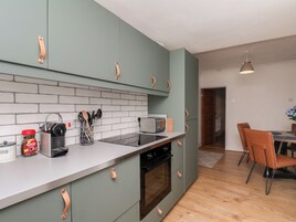Uma cozinha moderna com forno embutido, máquina de café e torradeira. Há uma área de jantar com mesa e cadeiras.