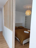 Quarto com cama, divisória de madeira, luminária pendente e armário branco.