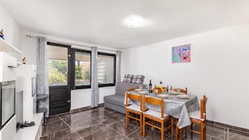 Uma sala de jantar com uma mesa posta para quatro pessoas, um sofá, uma TV e uma porta que dá para o exterior.