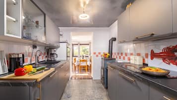 Uma cozinha moderna com armários escuros, uma ilha central e uma área de refeições visível através de uma porta aberta.