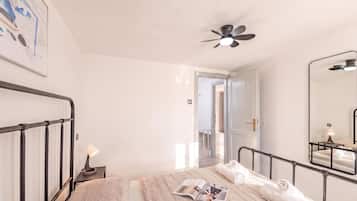 Quarto com cama, abajur, ventilador de teto, espelho e porta que dá para outro cômodo.