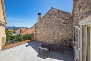 Uma varanda com parede de pedra, uma mesa e uma cadeira.