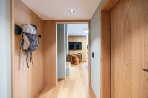 Um corredor com paredes de madeira, uma mochila pendurada na parede e vista para um quarto com sofá e televisão.