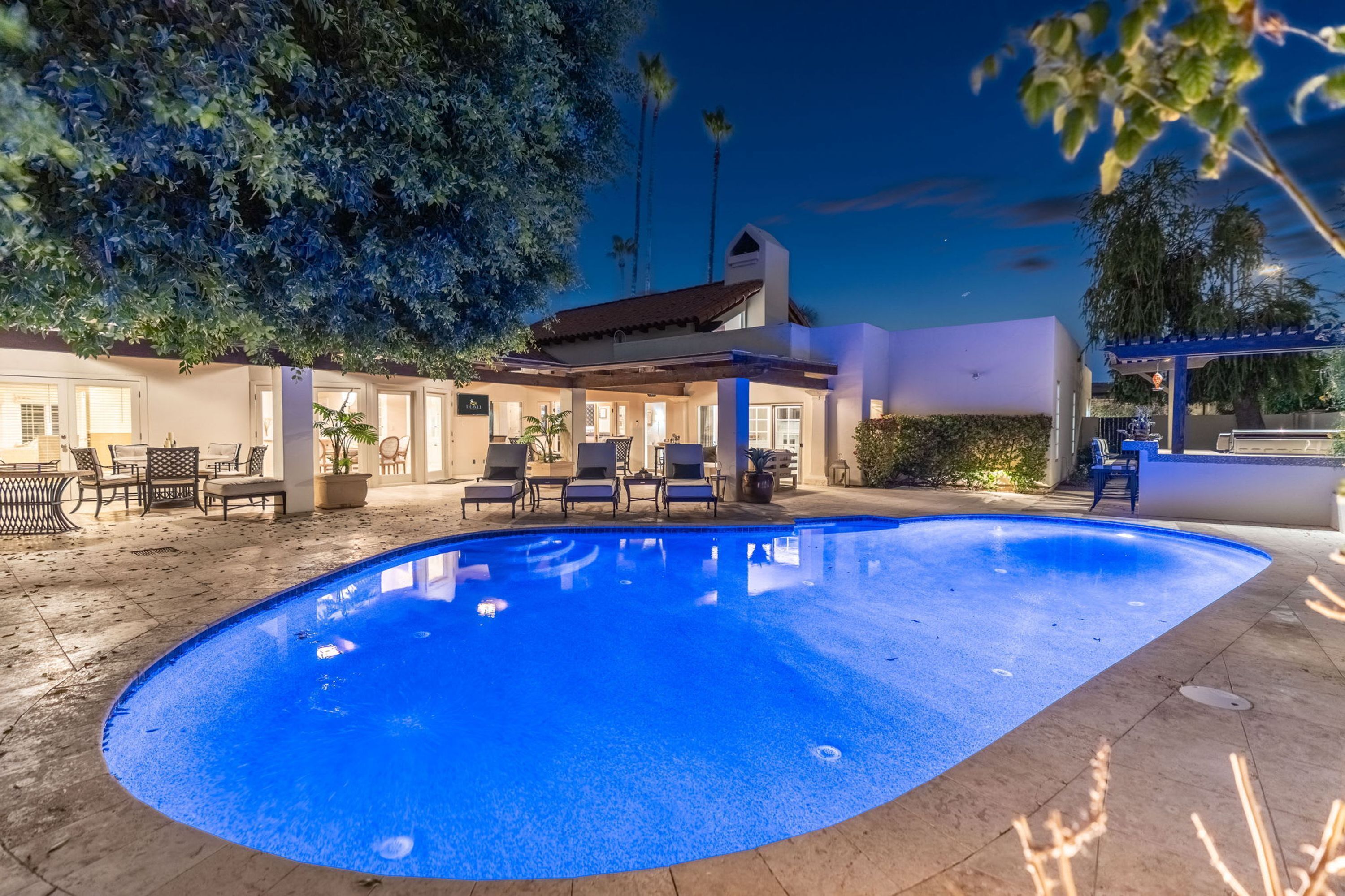 Piscina com espreguiçadeiras, alpendre coberto e edifício com fachada branca.