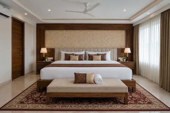 Quarto de hotel com uma cama grande, duas mesas de cabeceira com luminárias, um ventilador de teto e um tapete vermelho estampado.