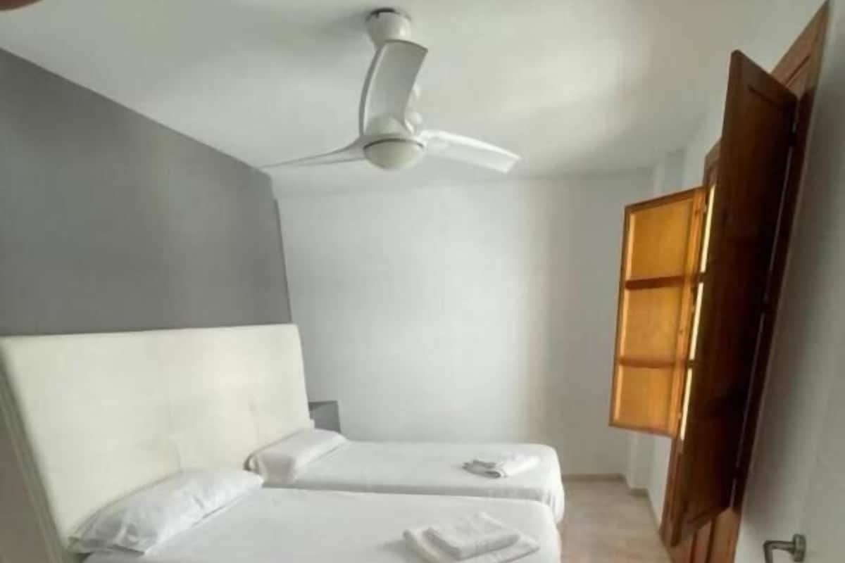 Quarto com duas camas, um ventilador de teto e uma porta de madeira.