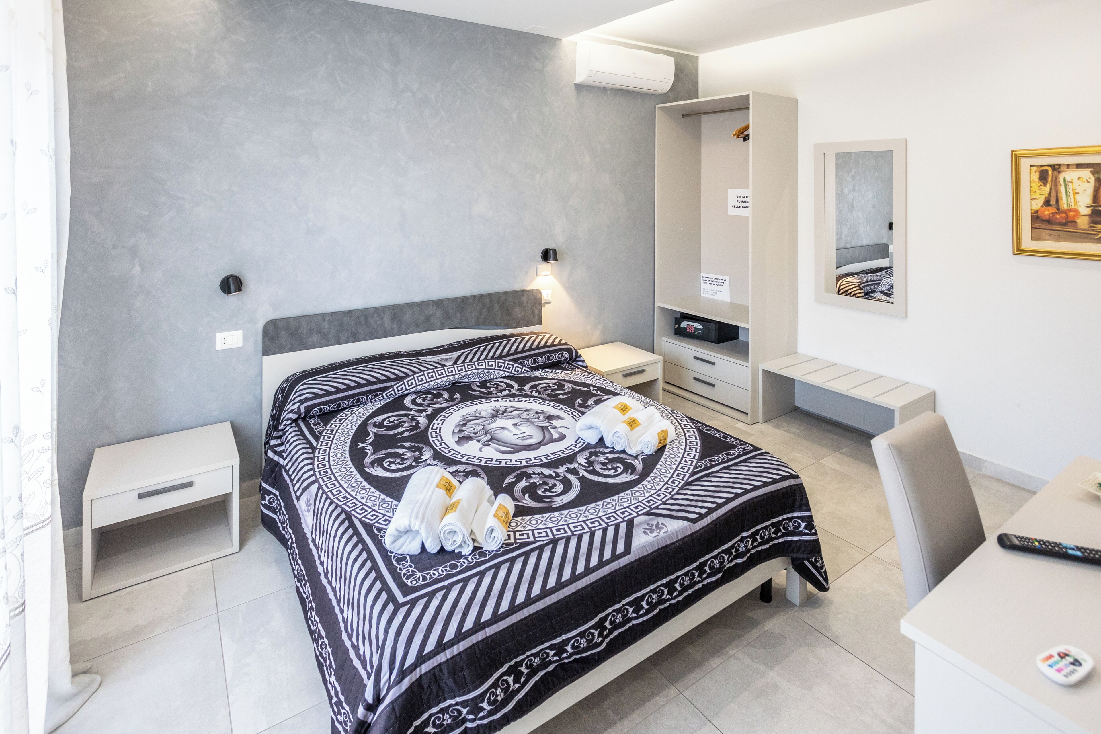 Quarto de hotel moderno com uma cama grande, mesas de cabeceira, escrivaninha e guarda-roupa.