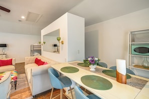 Uma sala de estar moderna com um sofá, uma mesa de jantar com cadeiras e uma área de cozinha com micro-ondas.
