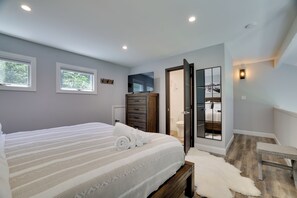 Quarto com uma cama grande, penteadeira de madeira, espelho e porta para um banheiro.