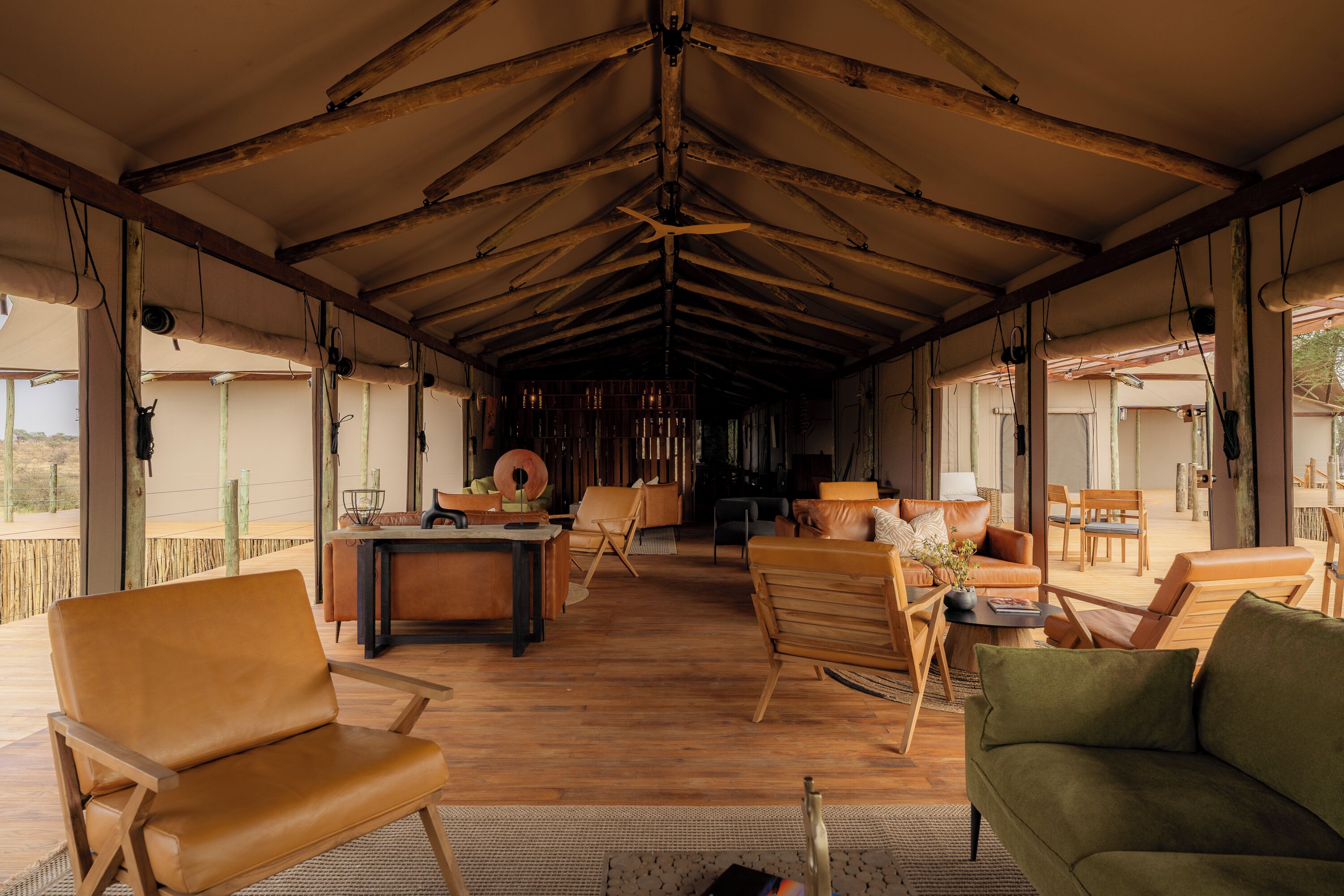 Amplo interior com teto alto e vigas de madeira, mobiliado com sofás e poltronas de couro, e uma mesa central.