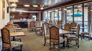 Um restaurante com mesas e cadeiras de madeira, janelas amplas e um balcão.