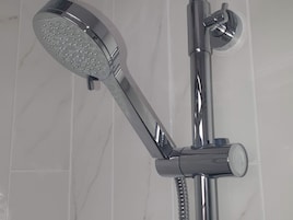 Um chuveiro cromado com design redondo e perfurado, fixo a um tubo vertical cromado com mangueira flexível.