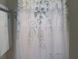 Casa de banho com cortina de chuveiro branca com padrão floral.