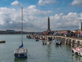 Um porto com barcos, um farol e um cais cheio de pessoas.