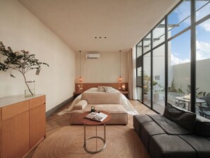 Quarto de hotel moderno com cama, sofá, mesa pequena e uma grande janela com vista para o exterior.