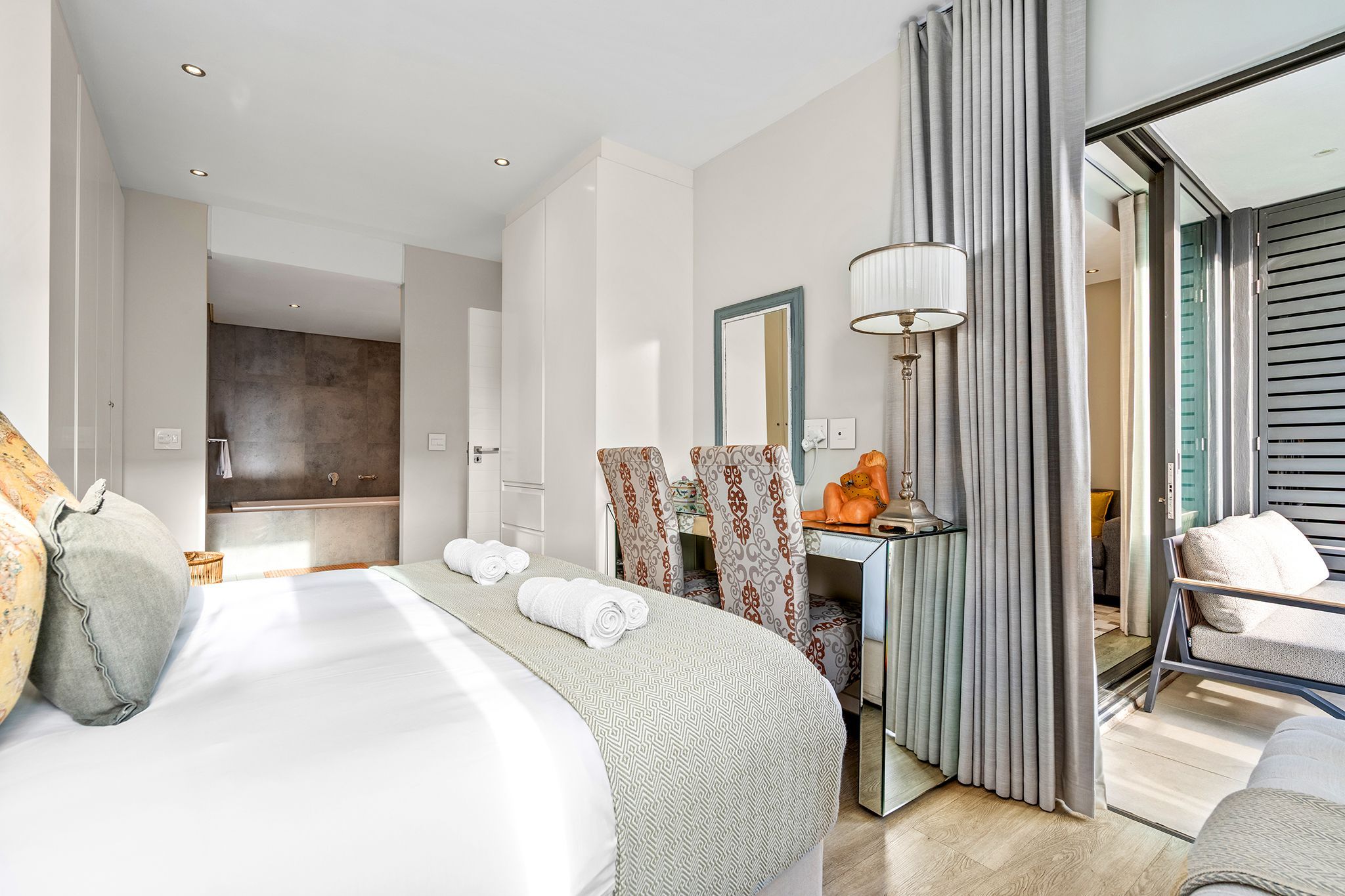Quarto de hotel moderno com uma cama grande, uma escrivaninha, um espelho e vista através de uma porta de correr.