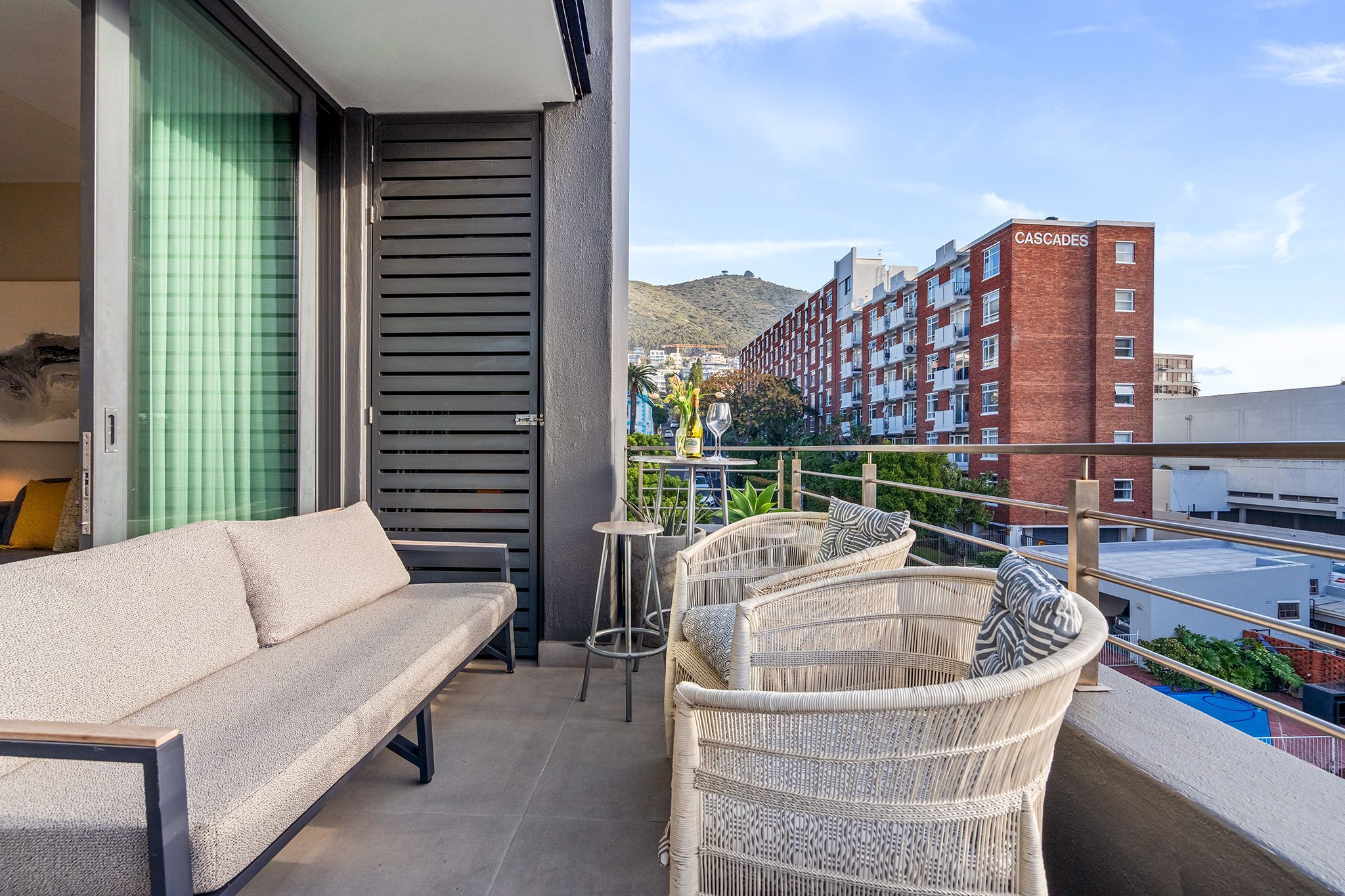 Uma varanda com sofá, cadeiras de vime e vista para um edifício identificado como 'Cascades'.