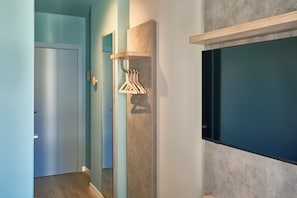 Um corredor com um porta-roupas de madeira, uma porta e uma televisão fixada na parede.