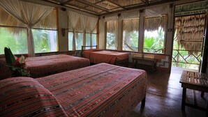 Quarto com quatro camas, janelas amplas e telhado de palha.