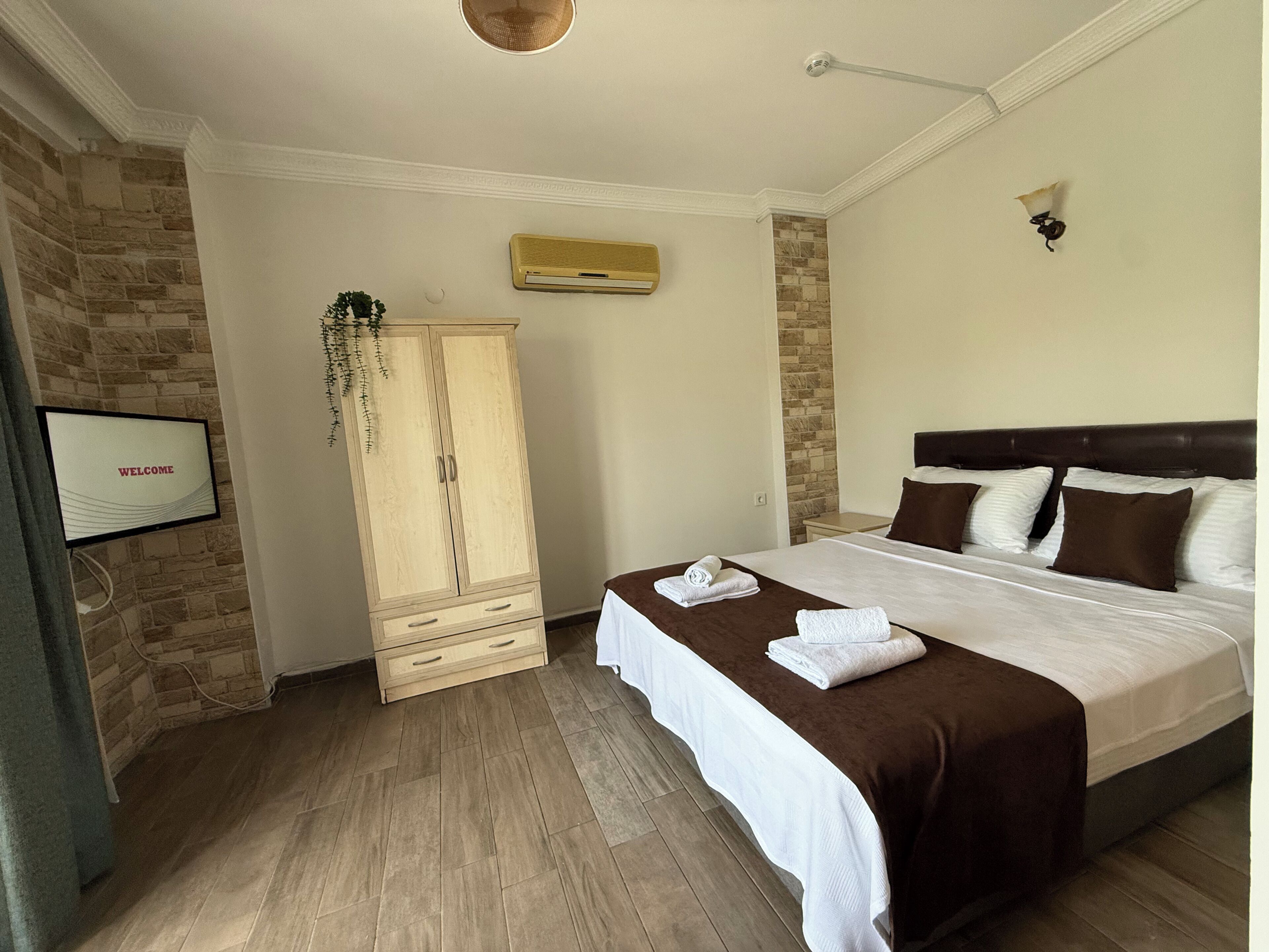 Quarto com cama, guarda-roupa, televisão e ar condicionado fixado na parede.